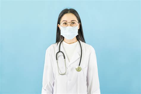 스마트 젊은 아시아 여자 의사 에 실험실 코트 와 의료 얼굴 마스크 흰색 라텍스 의료 장갑 과 청진기 블루 배경 건강 관리 개념