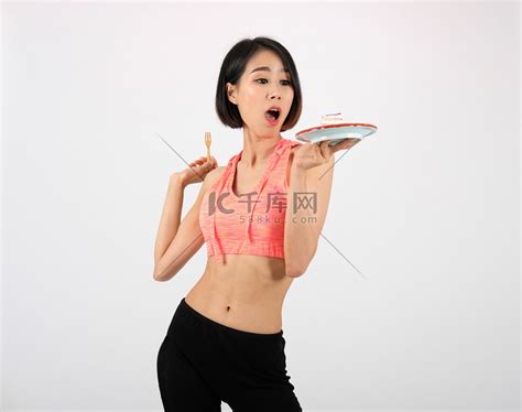 穿着运动服的运动健身女人在白色背景上吃蛋糕。高清摄影大图 千库网