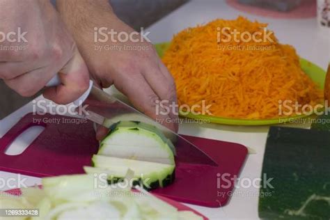 한 남자가 채소 골수를 갈고 닦는다 스쿼시 캐비어 를 요리하기위한 인근 야채 테이블 표면에 호박 당근 양파 토마토 건강한