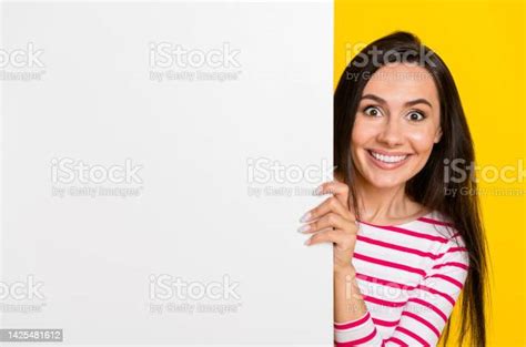 매력적인 젊은 여성의 사진 초상화는 노란색 배경에 고립 된 트렌디 한 줄무늬 모양을 입은 빈 흰색 빈 공간 뒤에 서 있습니다