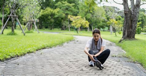 아시아의 매력적인 스포츠 여성은 거리에서 달리는 동안 발목에 통증을 느낀다 운동복을 입은 아름다운 소녀 운동 선수가 공원에서 운동 후 관절 인대 문제에서 다리를 마사지하고