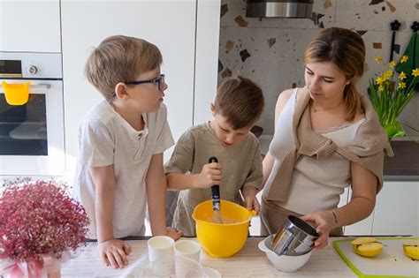 부엌에서 함께 빵을 굽고 있는 엄마와 아이들 어머니와 두 아들이 밝은 부엌에서 노란색 그릇에 재료를 섞고 밀가루를 체로 쳐서 함께 레시피를 만듭니다 3 명에 대한 스톡 사진