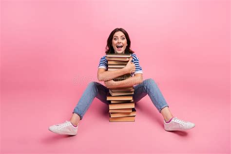 Happy Young Woman Sitting On Pink Background Hugging Large Stack Of Books With Excitement Stock