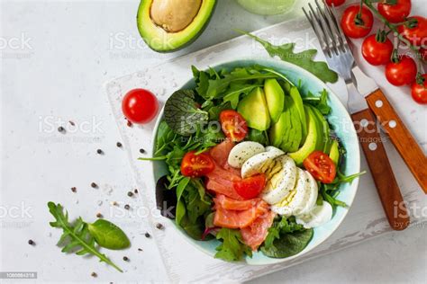 다이어트 메뉴 채식주의 음식입니다 Arugula 토마토 연어 계란 흰 돌 테이블에 아보카도 함께 건강 한 샐러드 탑 볼 평평