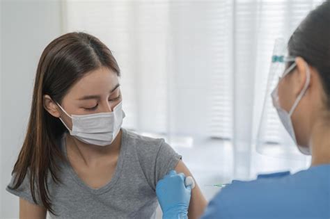 Covid 19、コロナウイルスのアジアの若い女性が、医師または看護師からワクチンを受け、腕の患者に注射を打った。予防接種、予防接種
