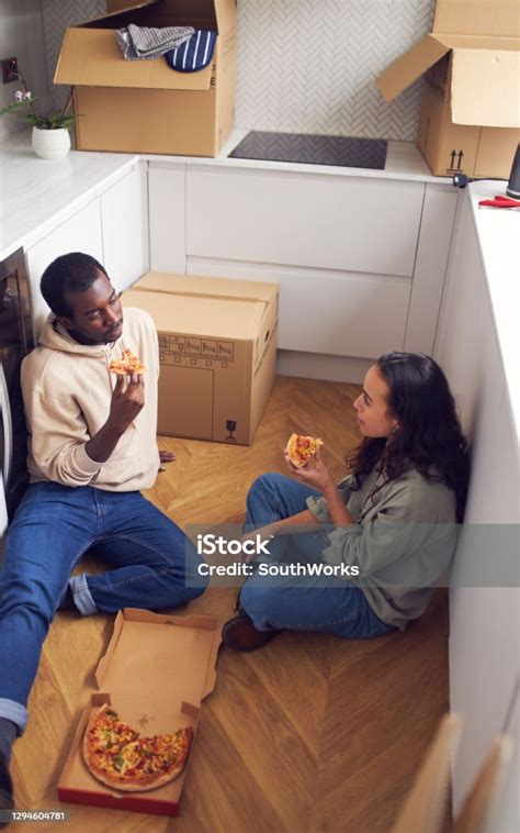 젊은 부부는 제거 상자와 부엌에서 피자를 먹고 바닥에 앉아 새로운 집으로 이동 축하 새 집으로 이사에 대한 스톡 사진 및 기타 이미지 새 집으로 이사 피자 젊은 커플
