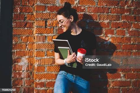 자유 시간 동안 광고 영역과 벽돌 벽에 대한 도시 설정에서 산책 쾌활한 매력적인 십대 행복한 여학생 에 안경 즐기는 휴식 야외 와 테이크 아웃 커피 감정에 대한 스톡 사진