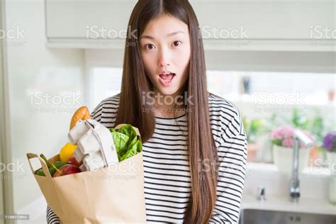 아름 다운 아시아 여자 신선한 식료품의 종이 봉지를 들고 놀라게 얼굴 충격에 무서 워 두려워 하 고 공포 표현으로 흥분 가방에
