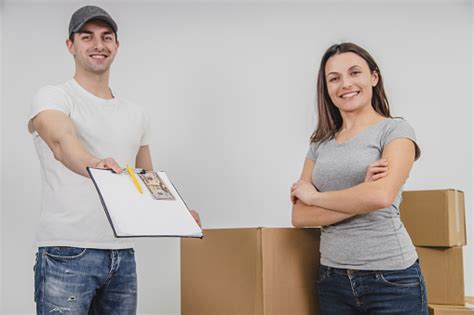 예쁜 여자와 택배 상자의 더미 근처 새로운 평면에 서 미소 그들의 거래에 만족 흐릿한 배달 남자가 서명 된 선언과 돈을 보여주고있다 2명에 대한 스톡 사진 및 기타 이미지