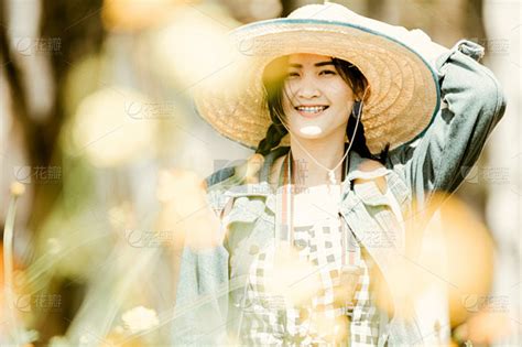 一名亚洲女子穿着格子衬衫，戴着草帽，在花丛中漫步。生态旅游的概念