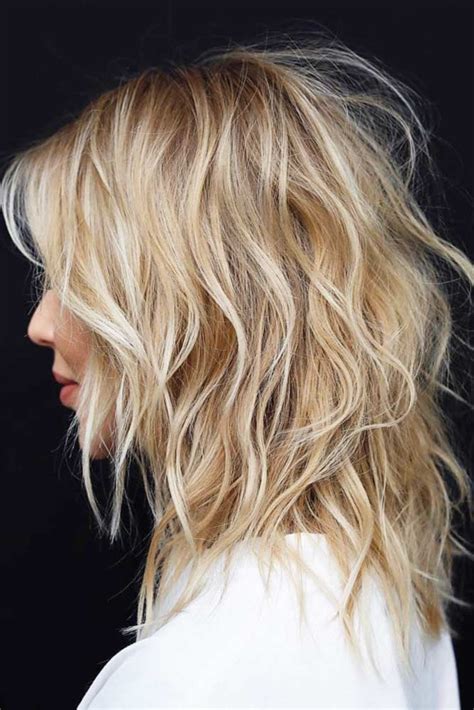 A Blonde Haired Woman With Wavy Hair Is Looking Off To The Side And Has Long Bangs