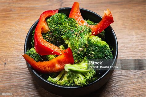 육즙이 풍부한 브로콜리 꽃과 생생한 빨간 피망 조각을 나무 테이블 위의 검은 그릇에 넣고 향신료를 뿌렸습니다 건강한 생활방식에 대한 스톡 사진 및 기타 이미지 Istock
