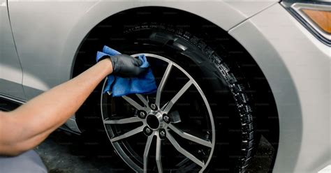 자동차 림 청소 자동차 세부 세차 개념 세차 서비스에서 파란색 극세사 천으로 세차 합금 휠을 씻은 검은색 고무 장갑을 낀 남성 손의 자른 클로즈업 사진 사진