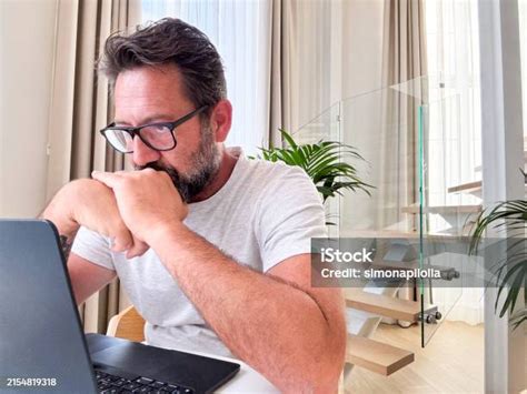 열린 노트북 컴퓨터 앞에서 걱정스러운 표정으로 화면을 바라보고 있는 사려 깊은 남자 온라인 작업을 하는 사람과 문제 여행자 유목민을 위한 호텔 방 배경의 계단과 창문 가정