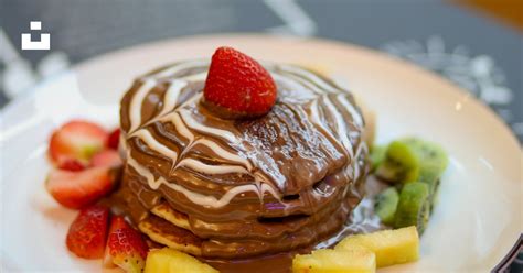 초콜릿 프로스팅과 과일로 덮인 팬케이크 더미를 얹은 흰색 접시 사진 Unsplash의 무료 미식가 이미지