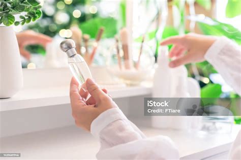 메이크업 액세서리와 테이블 미러와 함께 드레싱 테이블 근처에 앉아 그녀의 손에 향수를 적용 하는 여자 토끼 전구 유칼립투스 전나무 화병에 소나무 가지 개인 장식품에 대한