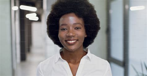 현대적인 사무실 건물 안에 서서 흰색 셔츠를 입고 카메라를 바라보며 아프리카 머리를 한 예쁜 웃는 흑인 젊은 여성의 얼굴