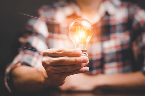 라인 연결이 있는 전구를 들고 책상에서 일하는 남자 손 창의성과 혁신은 성공의 열쇠입니다 에너지와 전력으로 새로운 아이디어와 혁신의 개념 집에서 일하는 프리미엄 사진