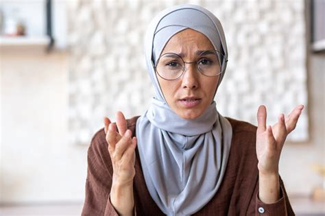 히잡과 안경을 쓴 젊은 무슬림 여성이 카메라를 진지하게 바라보며 영상 통화로 이야기하는 클로즈업 사진 설명 조언 손으로 제스처