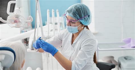 안면 마스크와 불룩한 모자를 쓴 신중한 여성 치열 교정 의사가 치과 드릴 머리 안에 새 강철 버를 배치합니다 사진 Unsplash의 건강 검진 이미지