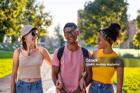 도시 공원에서 걷고 있는 Z 세대의 행복한 사람들 잘생긴 청년이 웃으면서 그를 바라보는 두 명의 아름다운 여성 도시 여행과