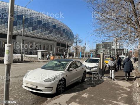 현대적인 새 경기장 근처의 무료 노상 주차장에서 테슬라 전기 자동차를 충전합니다 전기 자동차 개념에 대한 스톡 사진 및 기타