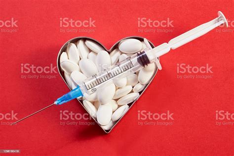 알약으로 만든 심장은 붉은 배경에 백신 주사기로 만든 화살표에 의해 관통된다 클로즈업 매크로 0명에 대한 스톡 사진 및 기타