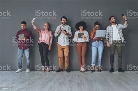 회색 배경에 디지털 장치를 사용하는 사람들의 다양한 그룹의 스튜디오 샷 다민족 그룹에 대한 스톡 사진 및 기타 이미지 다민족