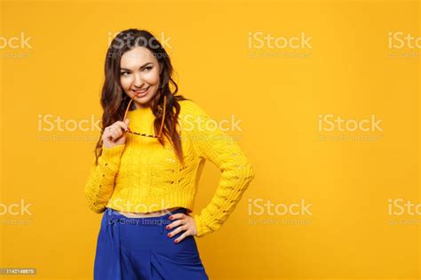 스웨터에 아름 다운 젊은 여자의 초상화 파란색 바지는 옆에 노란 오렌지 배경에 고립 된 보이는 안경을 들고 사람들은 진심으로