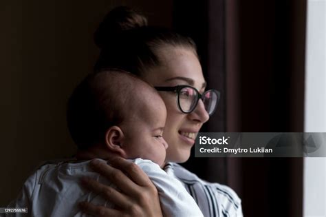 어린 시절 모성 가족 개념 성공적인 미소 부유 한 사업가 어머니 어머니가 그녀의 손에 유아 신생아를 들고 서서 실내 어두운 방에서 집에서 창문을 내려다 봅니다 가정 주방에