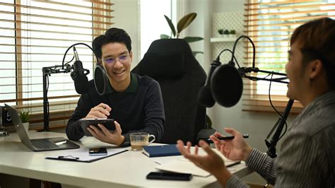 두 명의 행복한 팟캐스터가 콘덴서 마이크 앞에 앉아 현대적인 스튜디오에서 채널에 대한 대화를 녹음합니다 20 24세에 대한 스톡 사진 및 기타 이미지 Istock