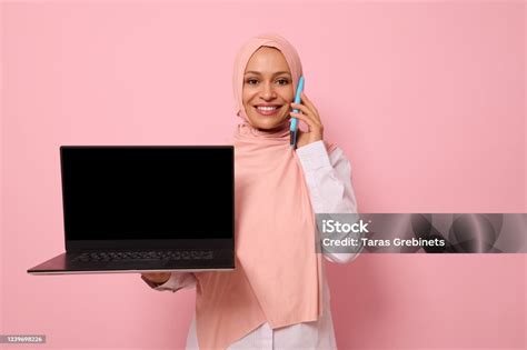 분홍색 히잡을 입은 예쁜 아랍 무슬림 여성이 휴대 전화로 이야기하고 이빨이 나는 미소로 미소를 지으며 카메라에 복사 공간이있는