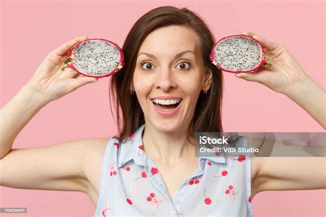 흥분 깜짝 젊은 여자 분홍색 파스텔 벽 배경에 고립 된 신선한 잘 익은 피타 야 용 과일의 절반을 들고 여름 옷에 사람들은