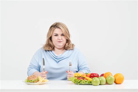 테이블에 흰색 바탕에 캐주얼 블루 옷에 젊은 매력적인 뚱뚱한 여자는 먹을 것을 선택 패스트 푸드 또는 건강 식품 다이어트와 적절