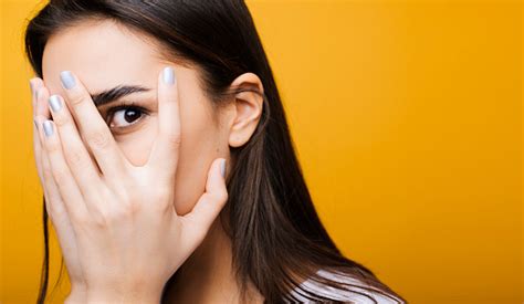 노란색 스튜디오 배경 앞에 손가락을 통해 카메라를 보면서 그녀의 손으로 얼굴을 숨기고 귀여운 젊은 유럽 여자의 초상화를 닫습니다 가리기에 대한 스톡 사진 및 기타 이미지