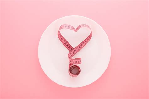 밝은 분홍색 테이블 배경에 흰색 접시에 측정 테이프로 만든 하트 모양입니다 파스텔 색상 근접 촬영 체중 감량 개념 하향식 보기 배경 주제에 대한 스톡 사진 및 기타 이미지