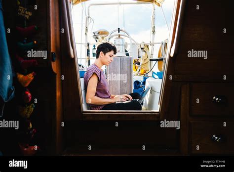Side View Of Woman Using Laptop Computer While Sitting In Boat Seen Through Window Stock Photo