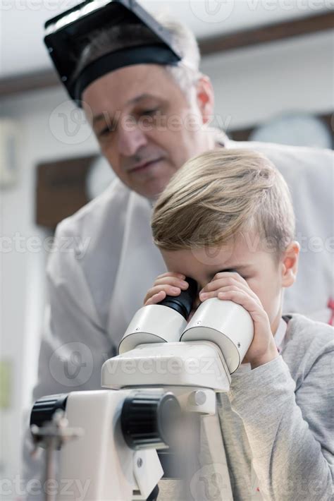 Little Boy Looking Through Microscope With Help Of A Teacher 10908953