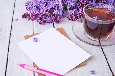나무 흰색 배경에 라일락 꽃차 한 잔 근처에는 종이 한 장과 분홍색 펜이 있습니다 엽서용 모캡 봄 시간 라일락을 곁들인 꽃병 텍스트공간을 복사합니다 휴일과 좋은 아침 소원의