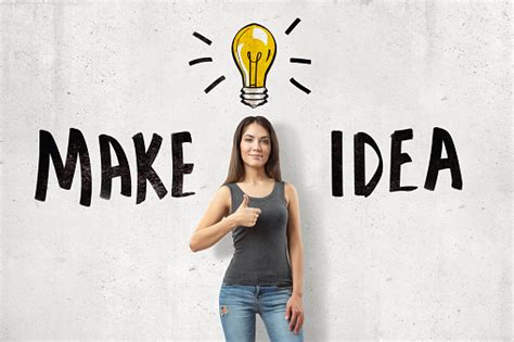 캐주얼 청바지와 티셔츠를 입고 젊은 갈색 머리 소녀는 흰색 벽 배경에 그려진 Make Idea기호와 만화 전구와 엄지 손가락을 보여주는 귀여운에 대한 스톡 사진 및 기타