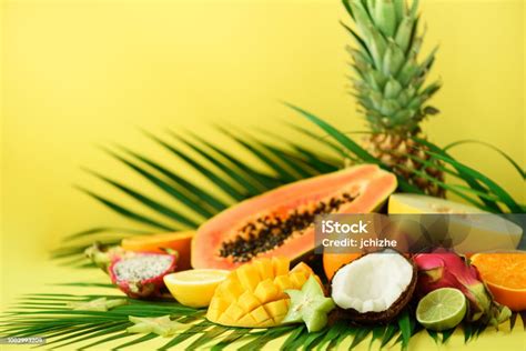 노란색 바탕에 이국적인 과일의 구색입니다 해독 채식주의 음식 여름 개념입니다 파파야 망고 파인애플 Carambola 드래곤 과일 키 위 오렌지 멜론 코코넛 팜 잎에 석 회