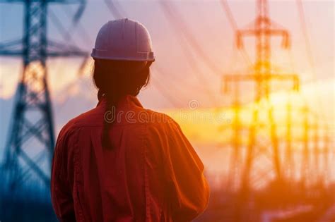 Female Engineer In Hard Hat Standing Before Power Lines At Sunset Energy Industry