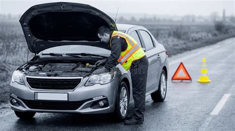 Man In Safety Vest Checks Car Engine Under Open Hood On Gray Road With