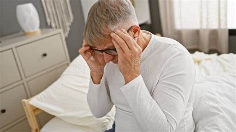 Gray Haired Man In Glasses Feeling Stressed Sitting On Bed In A Bedroom
