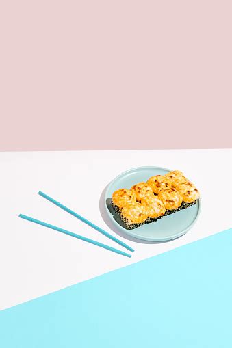 색깔이 있는 배경에 치즈와 참깨를 곁들인 뜨거운 마키 롤 구운 초밥 롤에 연어가 들어있고 참깨가 밖에 있고 치즈가 얹혀 있습니다 최소한의 스타일로 마키 초밥 일본 메뉴 개념