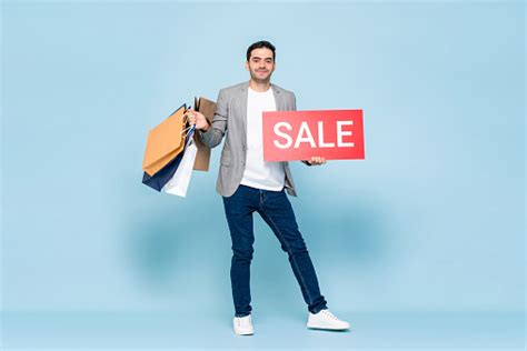 리외 밝은 파란색 스튜디오 배경에 서 쇼핑 백과 빨간 판매 기호를 들고 젊은 잘 생긴 백인 남자 전신에 대한 스톡 사진 및 기타 이미지 Istock