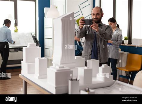 Architect Profession Man Looking At Maquette Layout Using Smartphone To Design Building Model