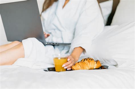 호텔 방 침대에서 아침 크루아상과 오렌지 주스를 가지고 노트북을 사용하여 흰색 가운에 긴 머리를 가진 젊은 아시아 소녀 20