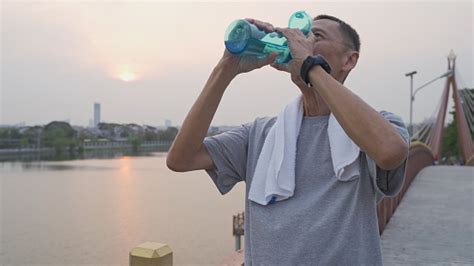 저녁 일몰에 현수교 공원에서 병에서 신선한 물을 마시는 목마른 아시아 활동적인 남자 성숙한 남성 음료 에너지 음료 다과 에서 피곤 하 고 운동에서 지친 2명에 대한 스톡