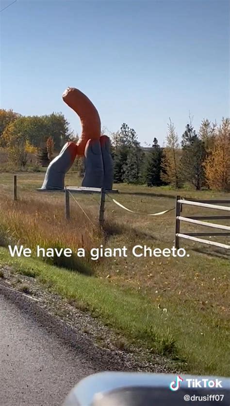 Giant Cheeto Held By Orange Fingertips Reaches For The Sky In Tiny Town